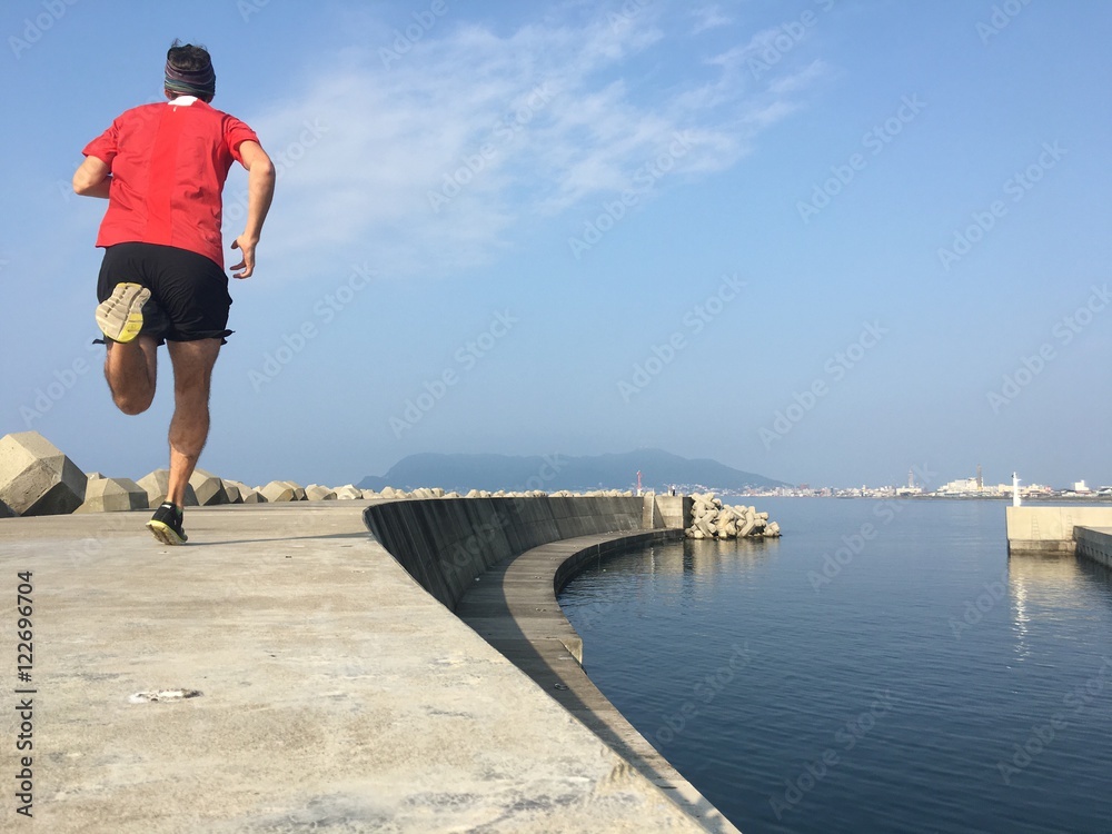 Male runner in red shirt on sea wall Stock Photo | Adobe Stock