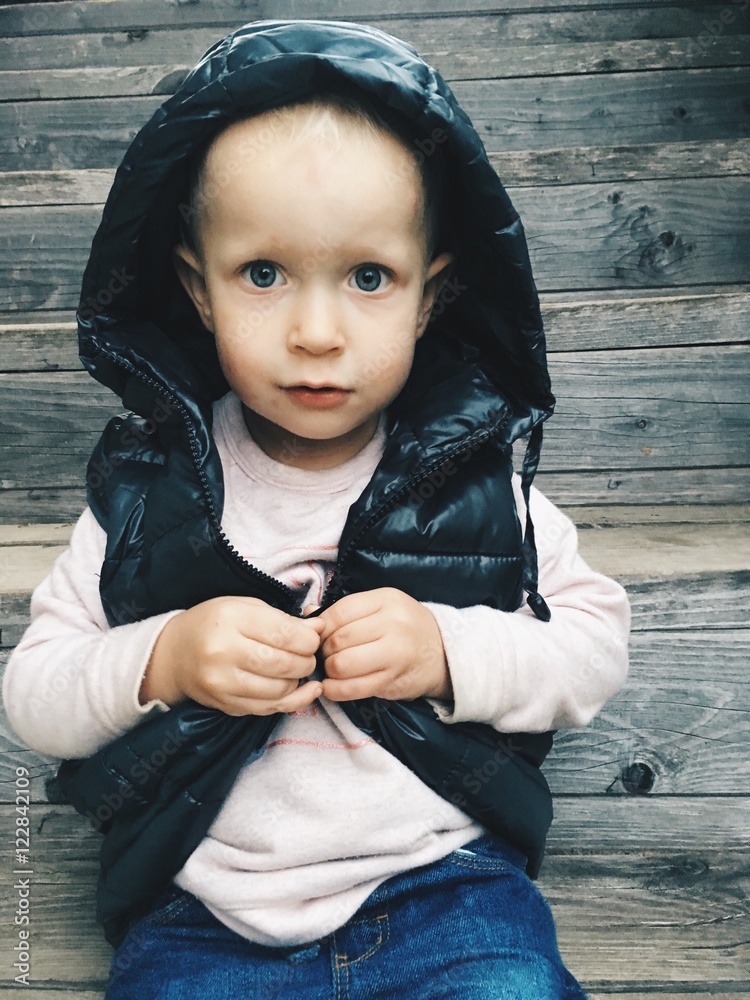 Child sitting outside country house in a village, wood wall background ...