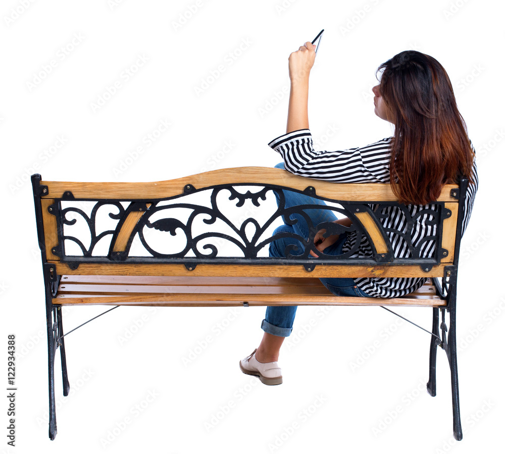 back view of woman sitting on bench and looks at the screen of the ...