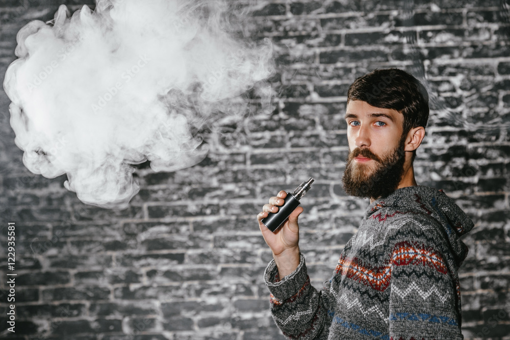Young man with beard vaping an electronic cigarette. Vaper hipster ...