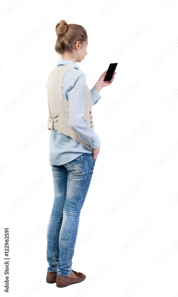 back view of standing young beautiful woman in vest and using a mobile ...