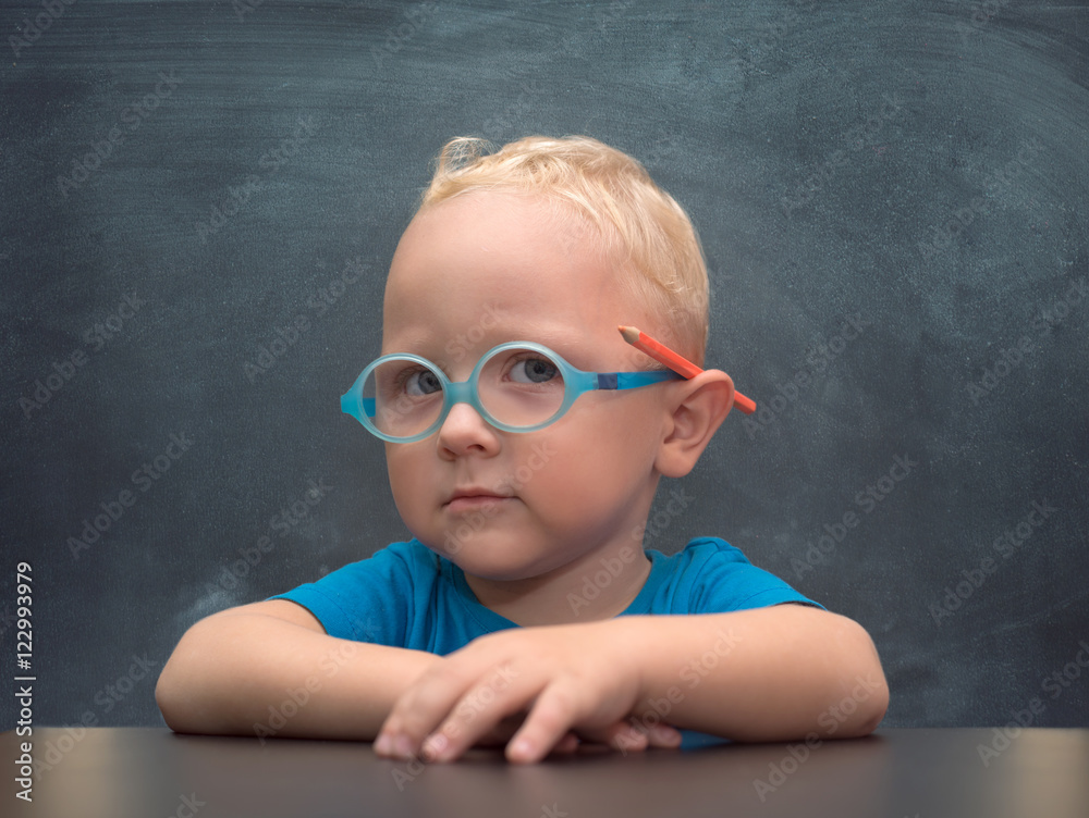 Smart kid wearing glasses with red pencil behind his ear sits at a ...