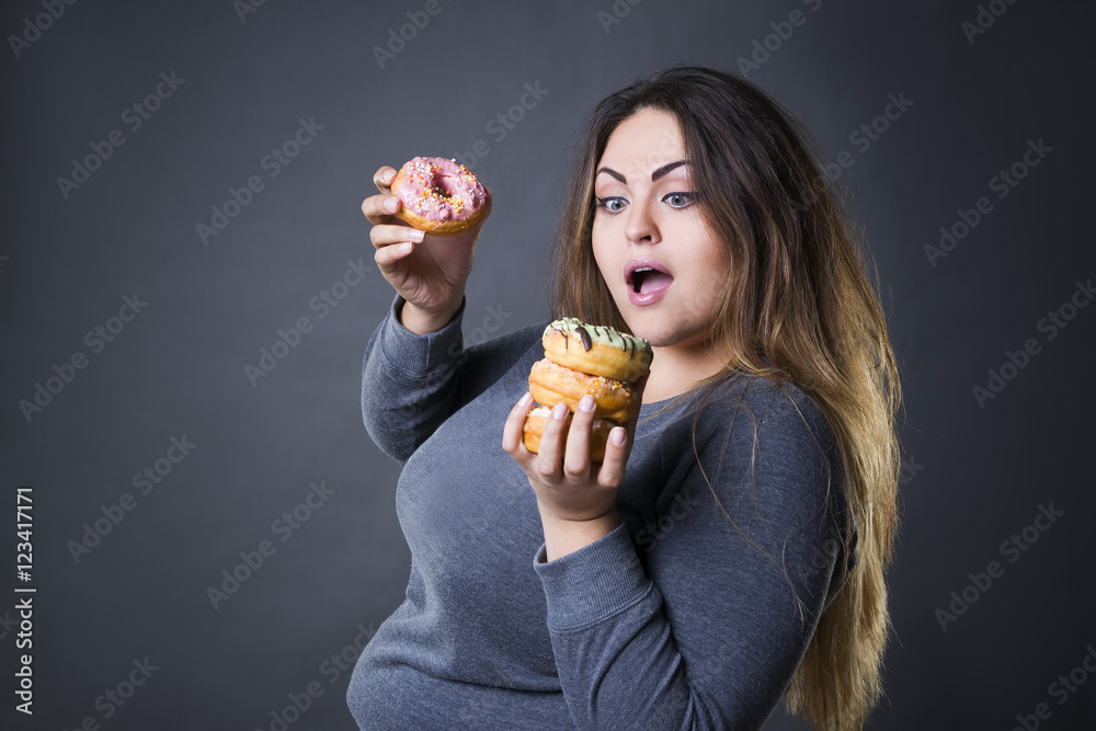 Beautiful young caucasian plus size model posing with donuts on a gray ...