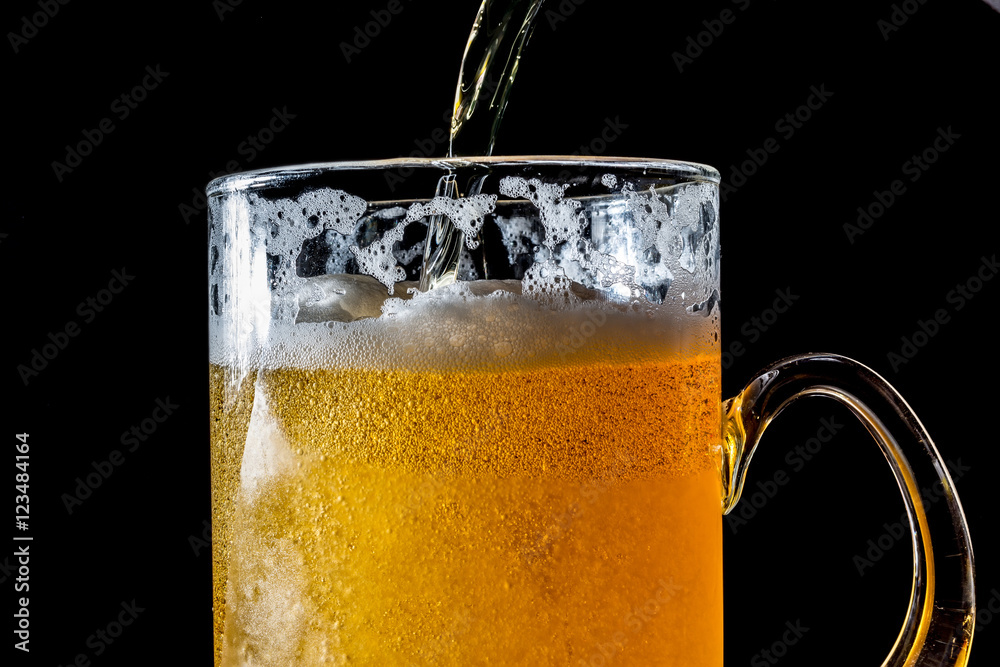 Stream of beer being pouring into a glass with beer and foam closeup ...