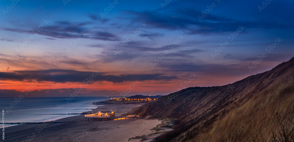 Beautiful sunset in the dunes at the beach with a beach club and ships ...