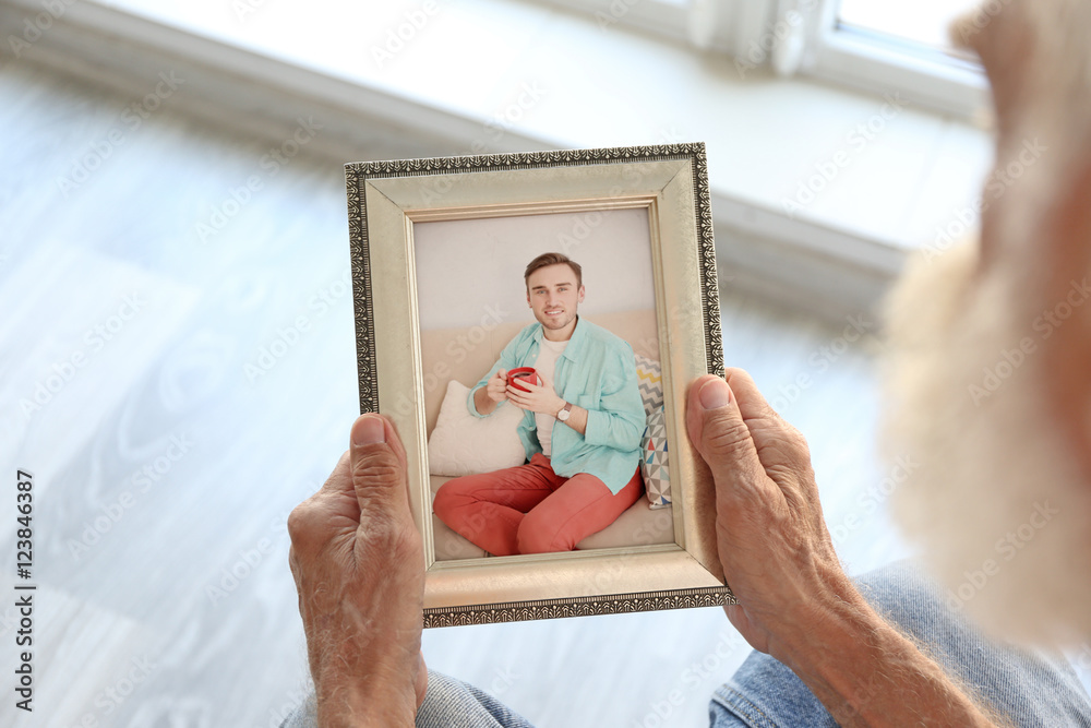 Elderly man holding photo frame with picture of grandson. Happy ...