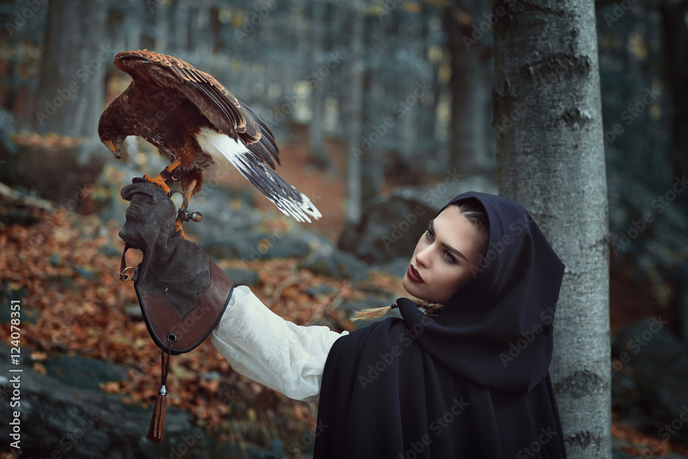 Foto Stock Beautiful huntress with hawk in a forest | Adobe Stock