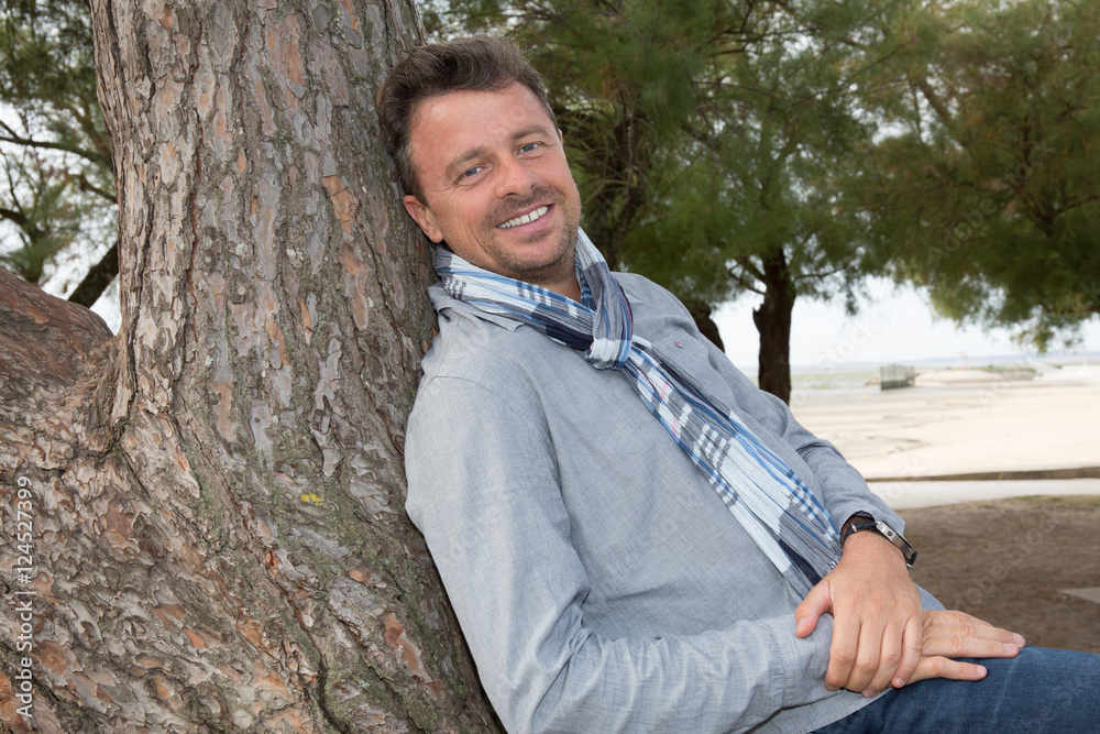 Smiling middle aged man relaxing In countryside leaning against tree ...