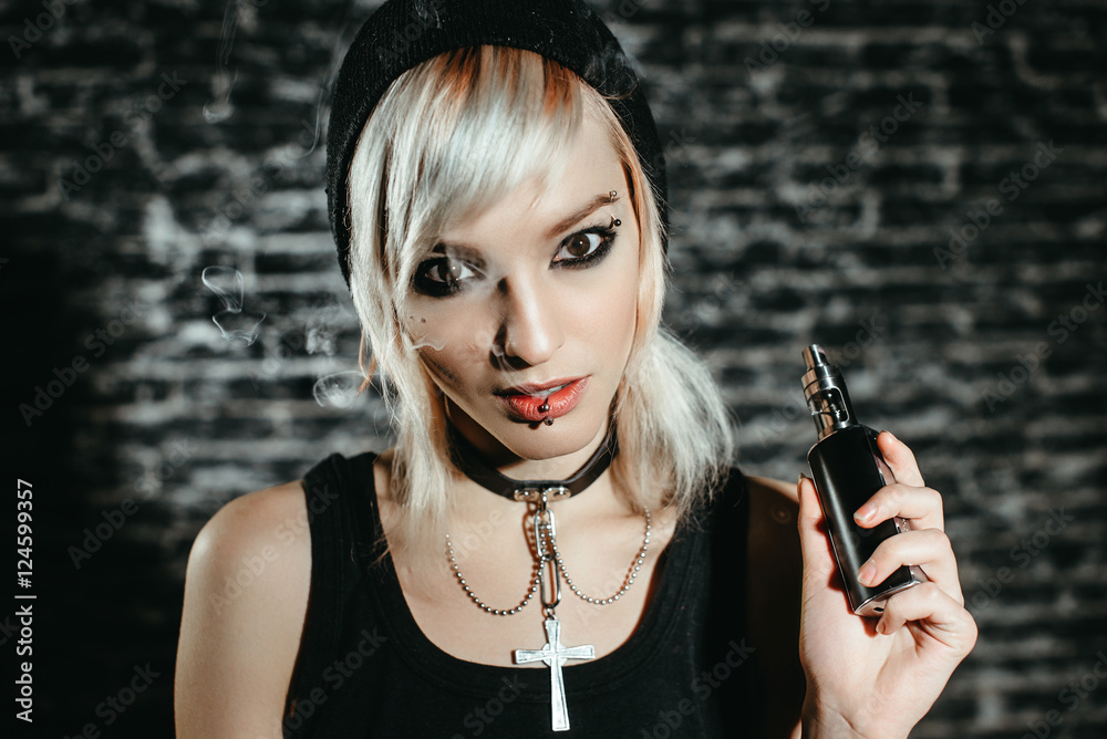 Sexy goth girl smokes electronic cigarette on dark background. The ...