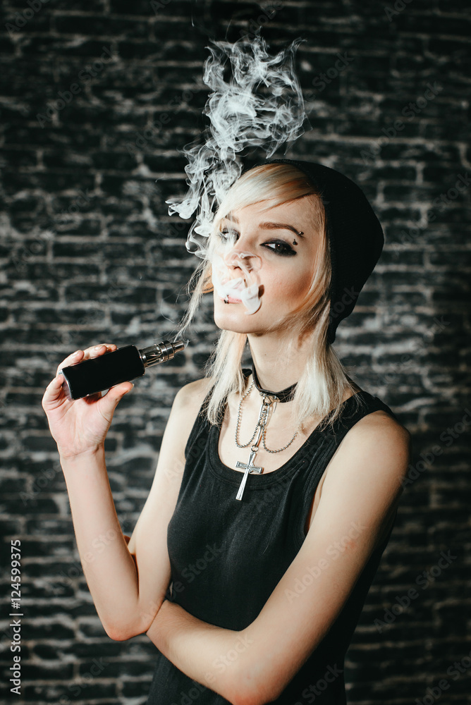 Sexy goth girl smokes electronic cigarette on dark background. The ...