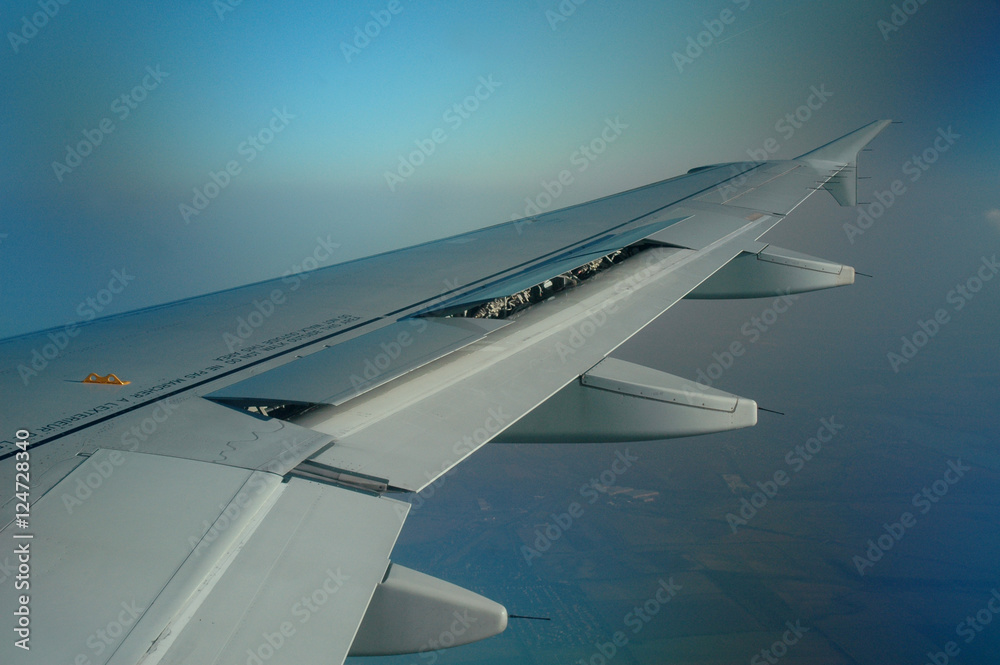 Aile d'avion en vol vue à travers un hublot passager, volets ouverts ...