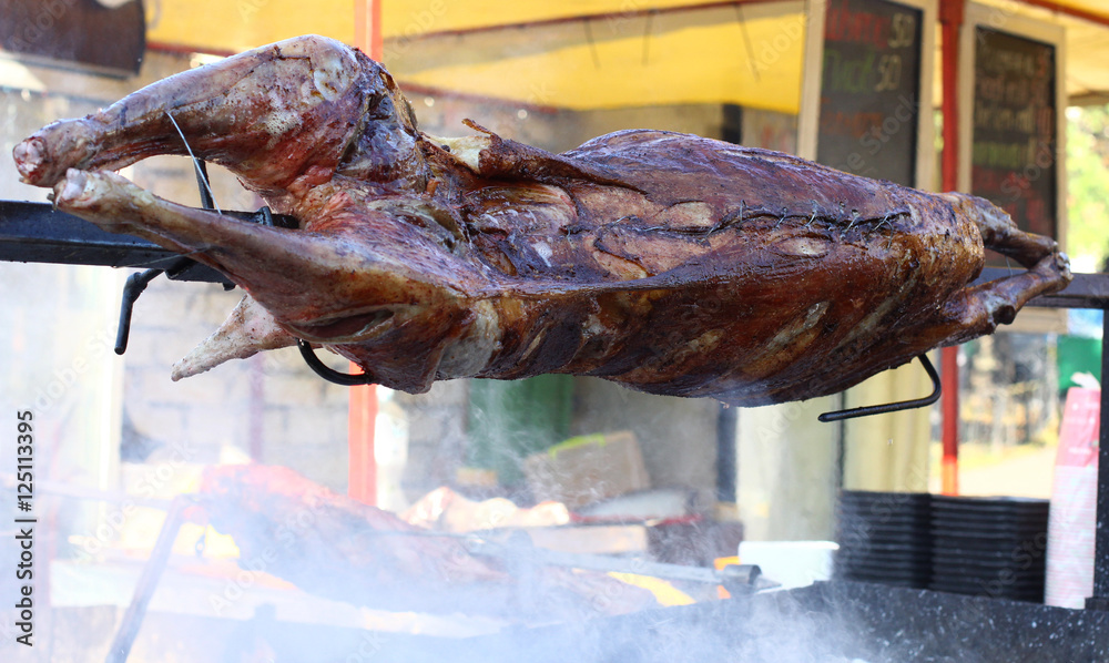 Carcass of a whole pork meat roasting on a spit over hot coals at an ...