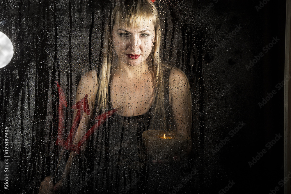Sweet female devil girl behind transparent glass covered by water drops ...