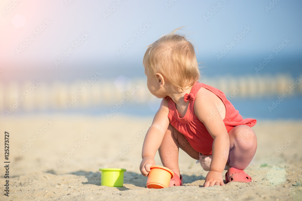 Baby playing on the sandy beach near the sea. Cute little girl in red ...