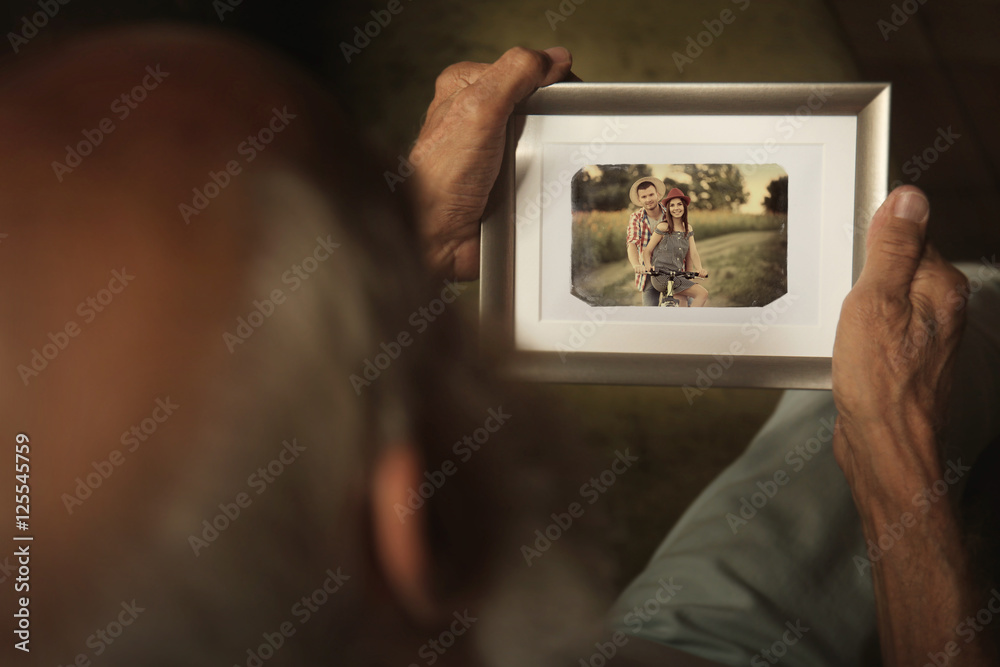 Elderly man holding photo frame with picture of young couple. Happy ...