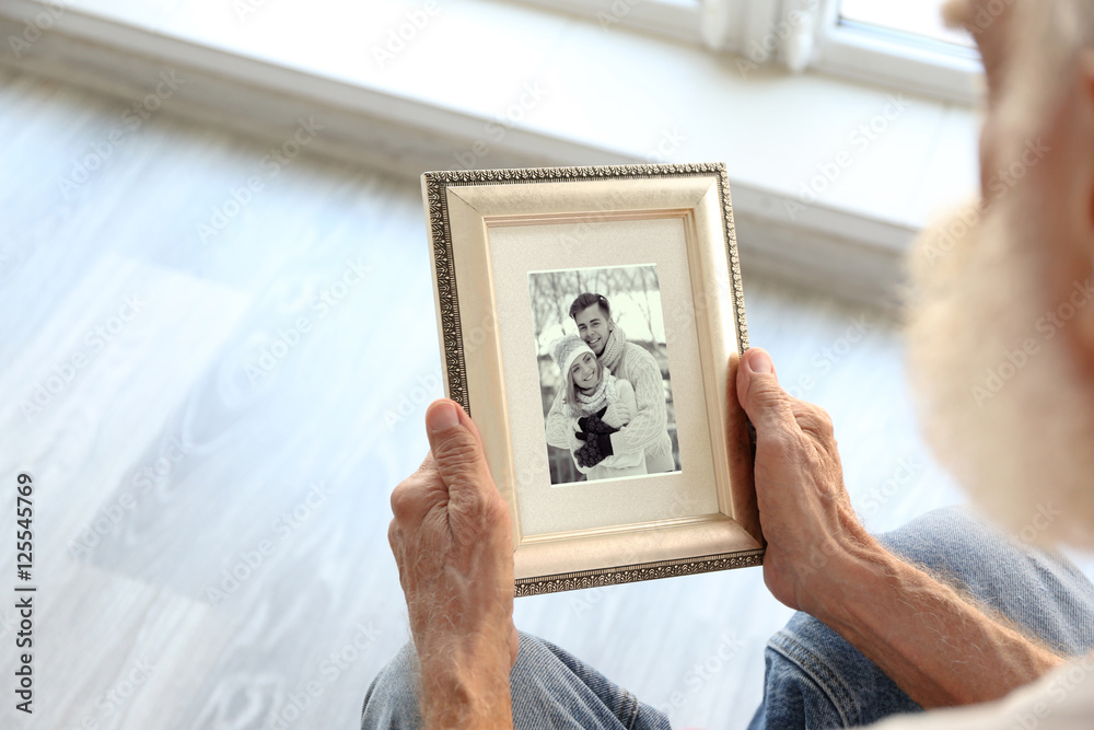 Elderly man holding photo frame with picture of young couple. Happy ...