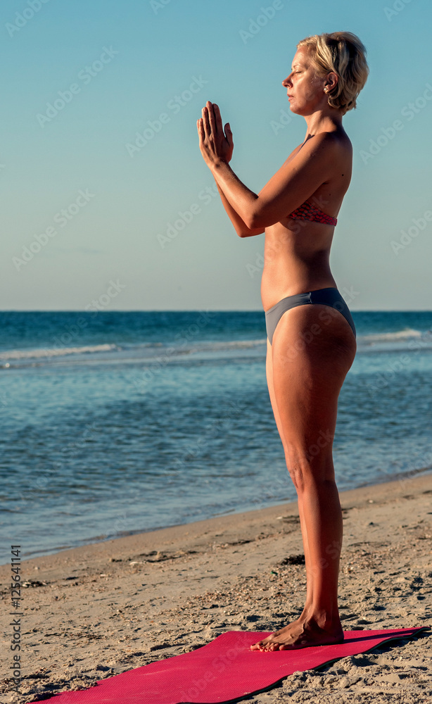 Middle-aged woman practicing yoga at the sea beach. At sunset, facing the sun.. Stock Photo ...