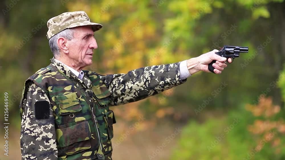Elderly person in military uniform shoots a revolver. Retired officer ...