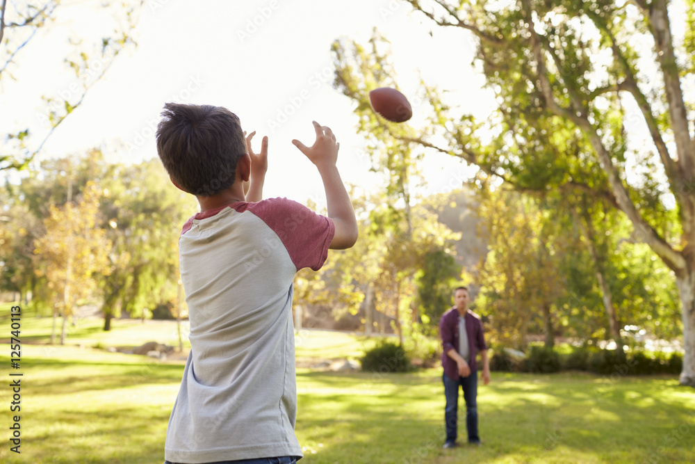 Foto de Dad and son throwing American football to each other in park do ...