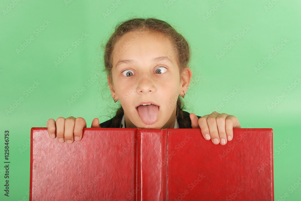 Beautiful school girl peeping from behind her red book. Pull a face ...
