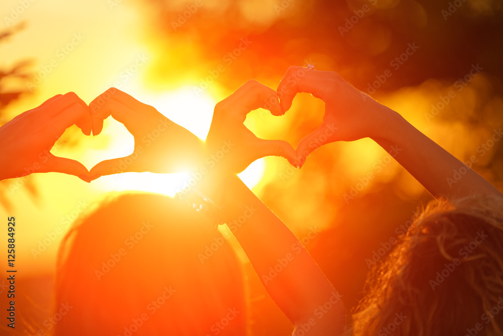 Girl-friends making a heart-shape for the sunset. Shallow depth of ...