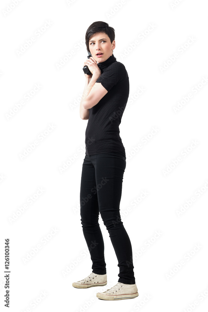 Side view of cautious female spy in black clothes with gun looking ...