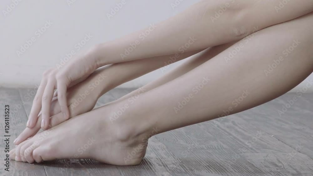 Woman gently touching her legs sitting on wooden floor with white wall ...