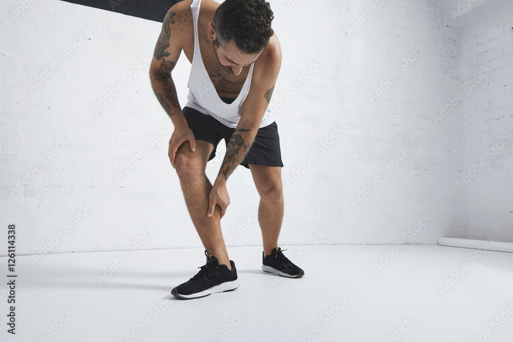 Athletic tattooed young man rubbing his injured during workout calf leg ...