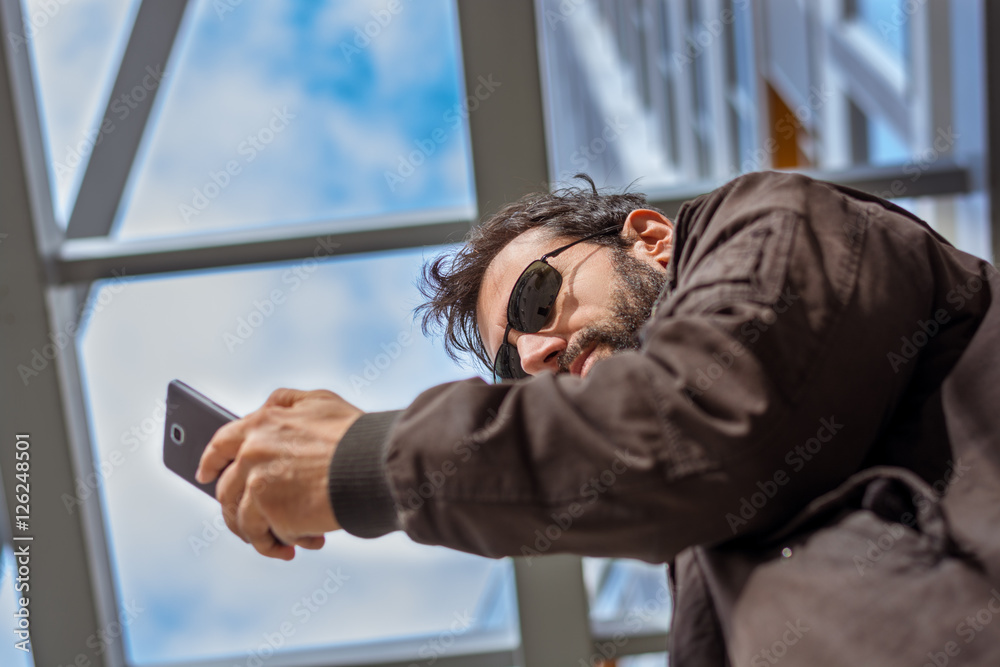 Handsome trendy man standing and looking down at a cell phone that he ...