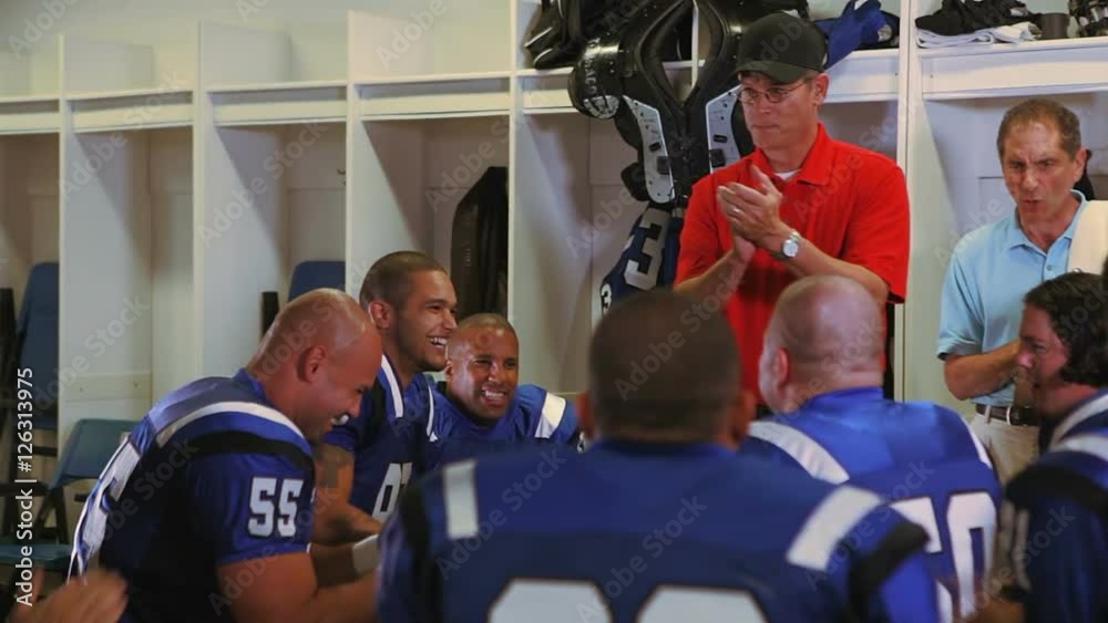 football team sits and claps in a circle in the locker room with their ...