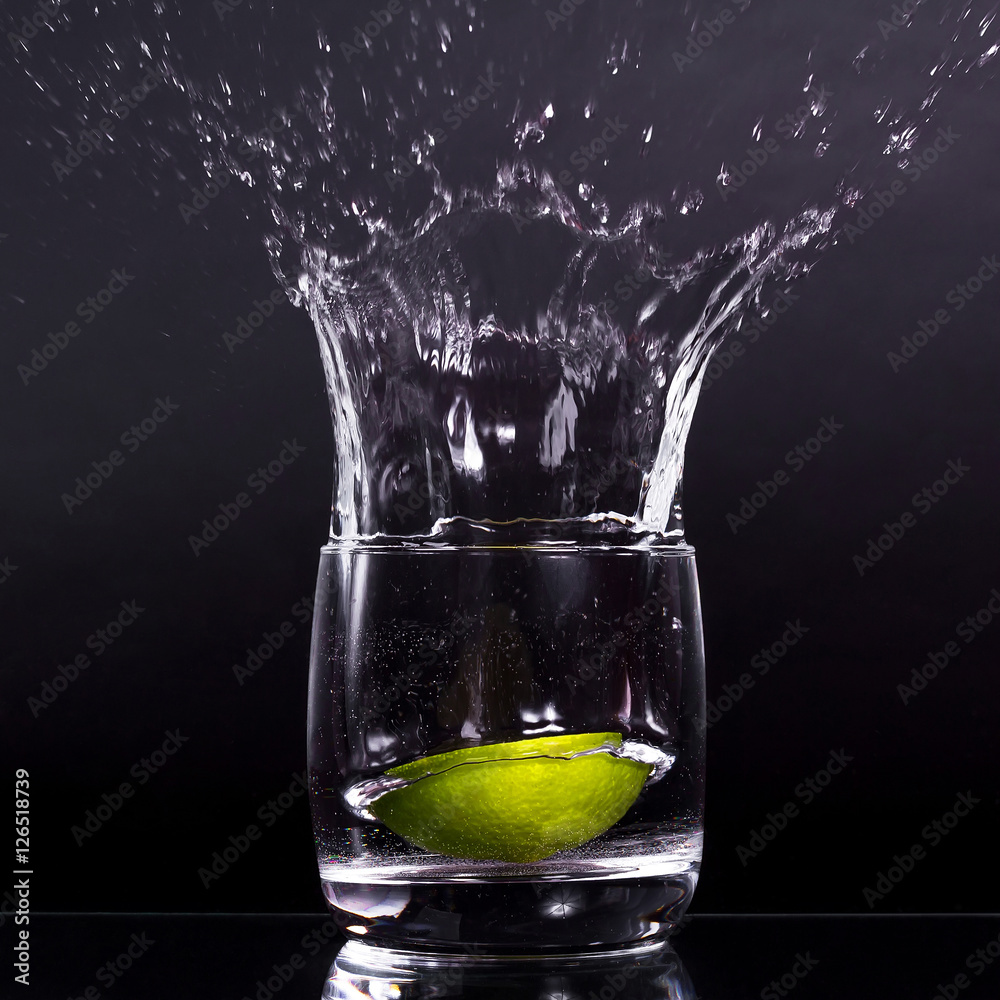 Falling in a glass of lemon, lime, splash on black background, isolated ...