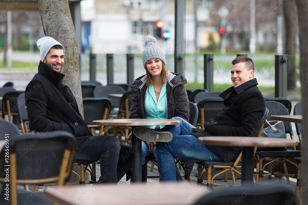 Three young happy friends sitting outside in a coffee shop and smiling ...