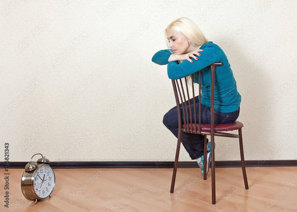 Sad girl sitting on a chair in an empty room and looks at his watch ...