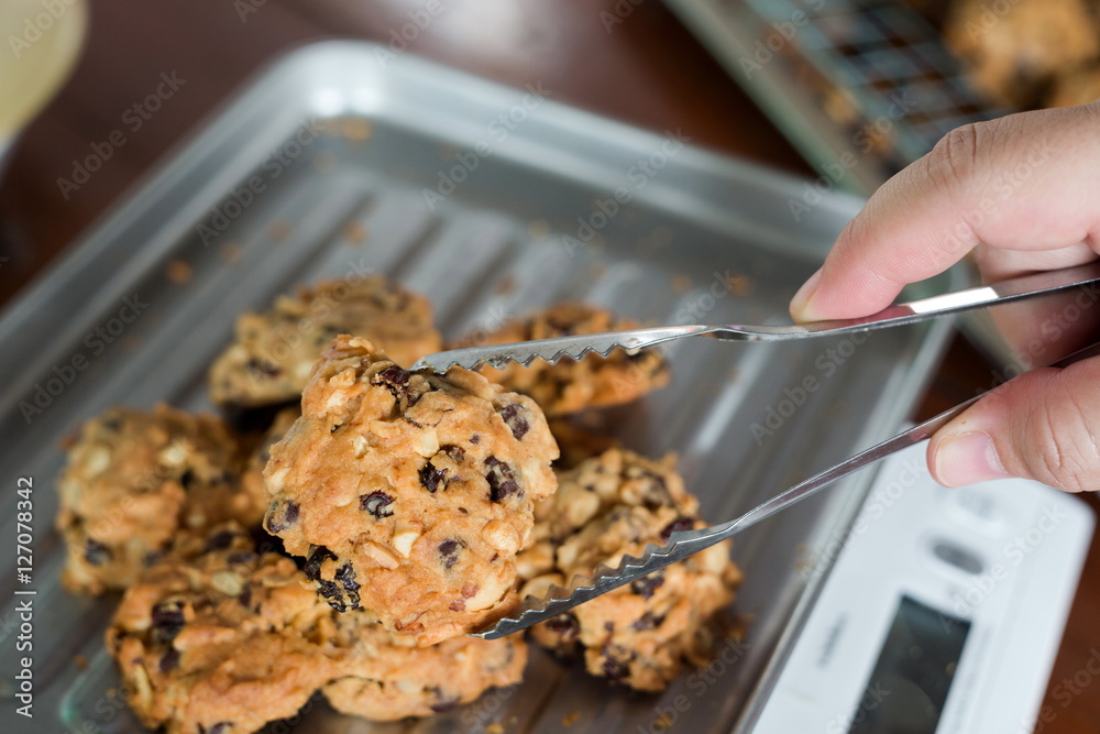 Hand holding cookies with stainless steel tongs. Stock Photo | Adobe Stock