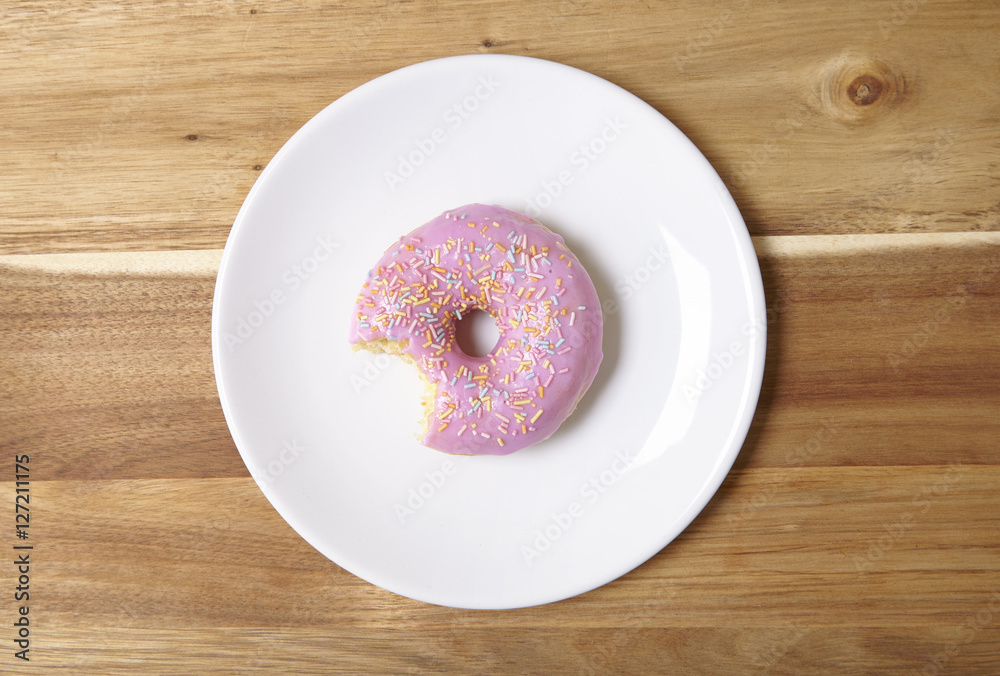 A ring doughnut with pastel pink frosting and sprinkles on a wooden ...