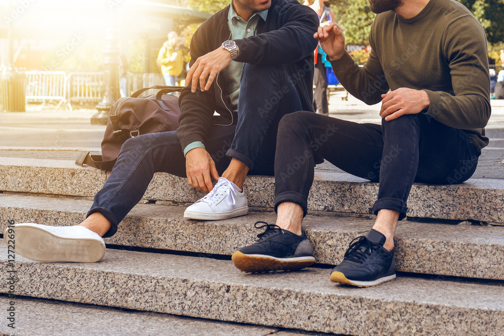 Lifestyle photo of two male friends sitting on the steps in city street ...