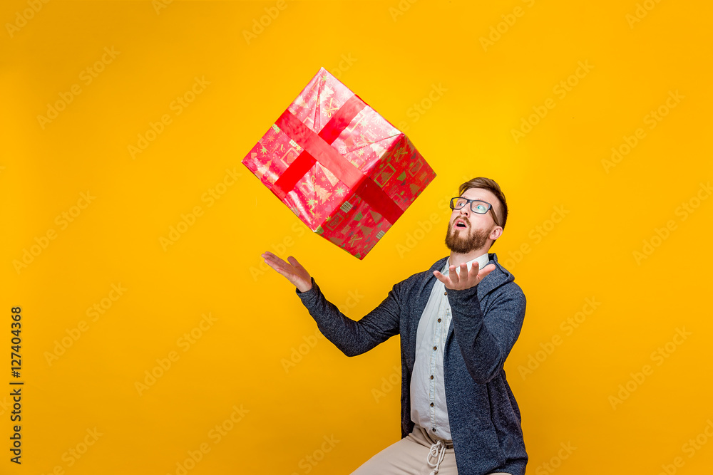 Young man looking casual in surprise throwing big red present gift box ...