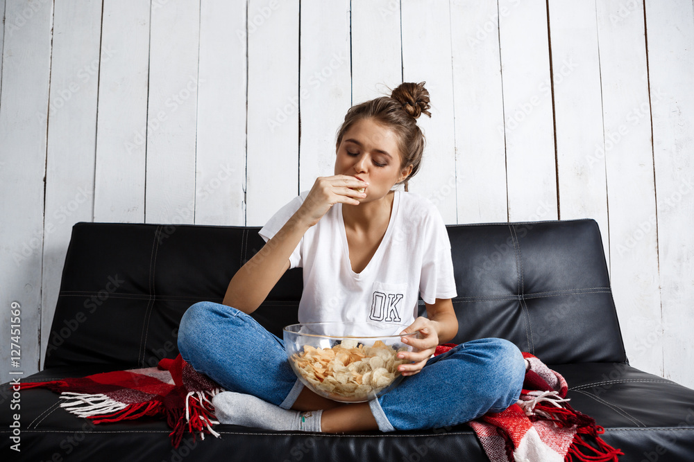 Beautiful domestic girl eating chips, watching tv, sitting at sofa ...