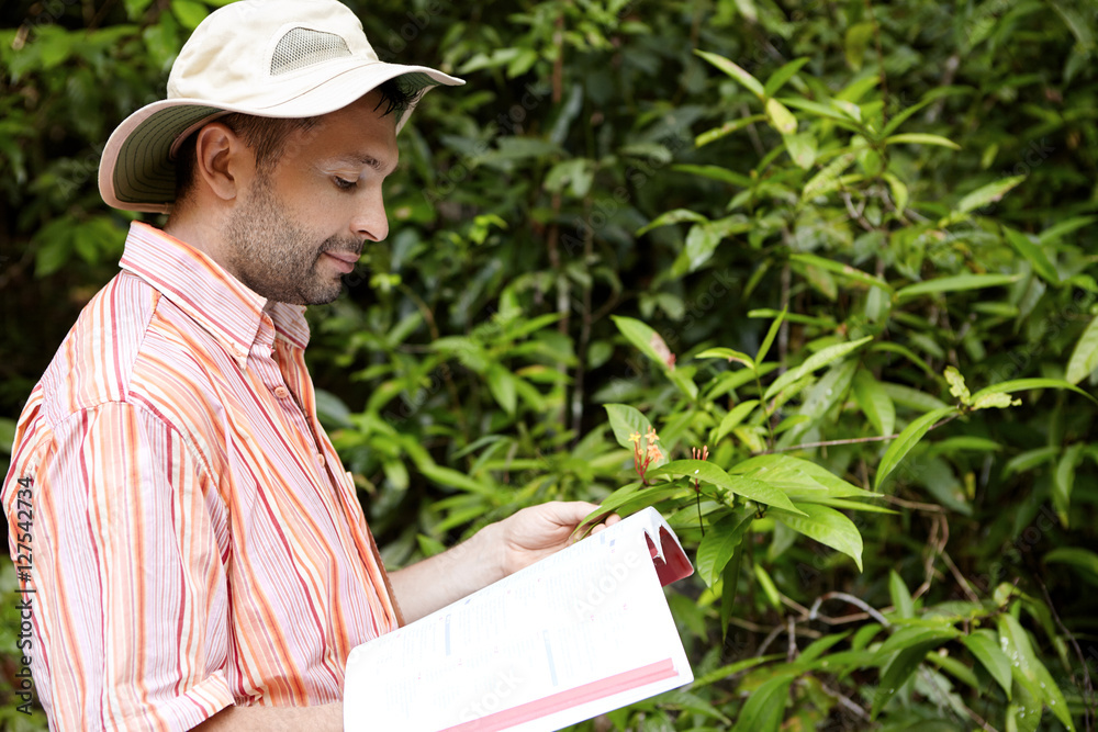 Handsome botanist with stubble wearing striped shirt holding manual or ...