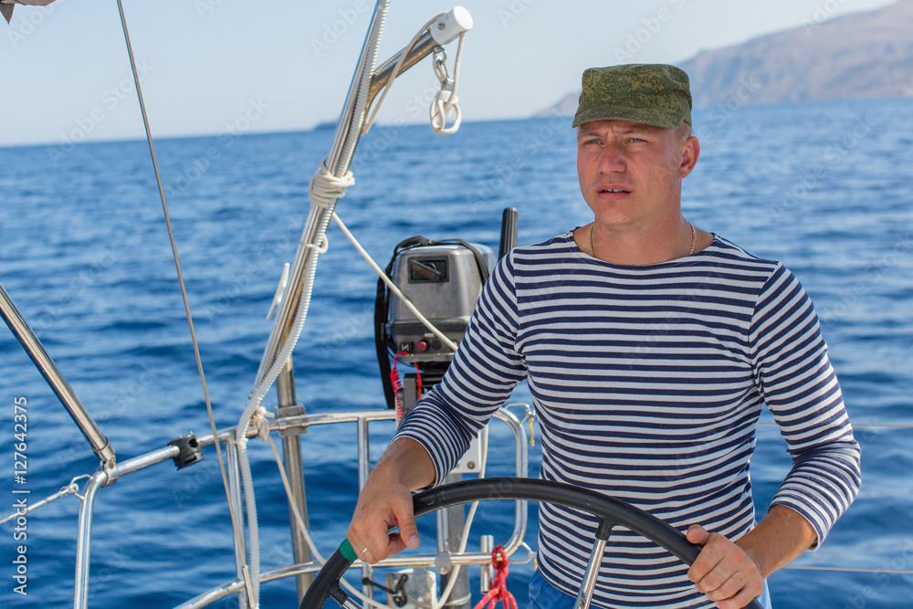 Young man skipper at the helm sail boat, controls ship during sea yacht ...