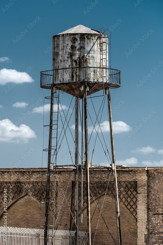 Old rusty water tower next to a brick wall blue sky sky utility ...
