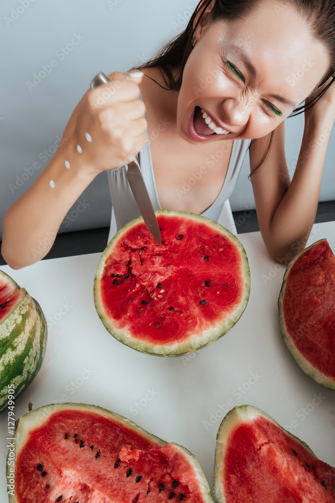 Mad irritated young woman screaming and cutting watermelon with knife ...