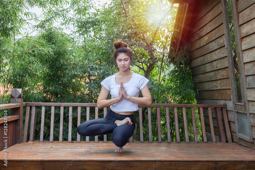 women relaxing in yoga toe stand pose on wooden terrace with warm light ...