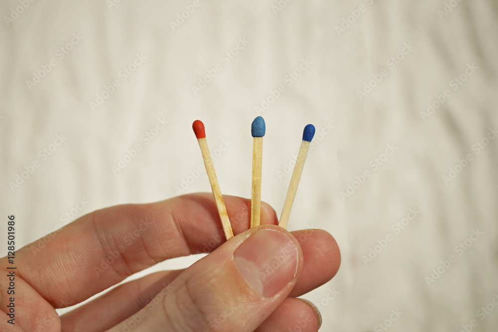 Male hand holding three safety matches, each with a different color of ...