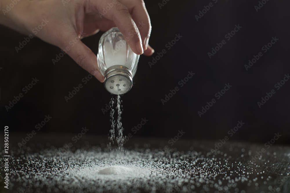 Adding salt. Backlight to salt from salt shaker. Stock Photo | Adobe Stock