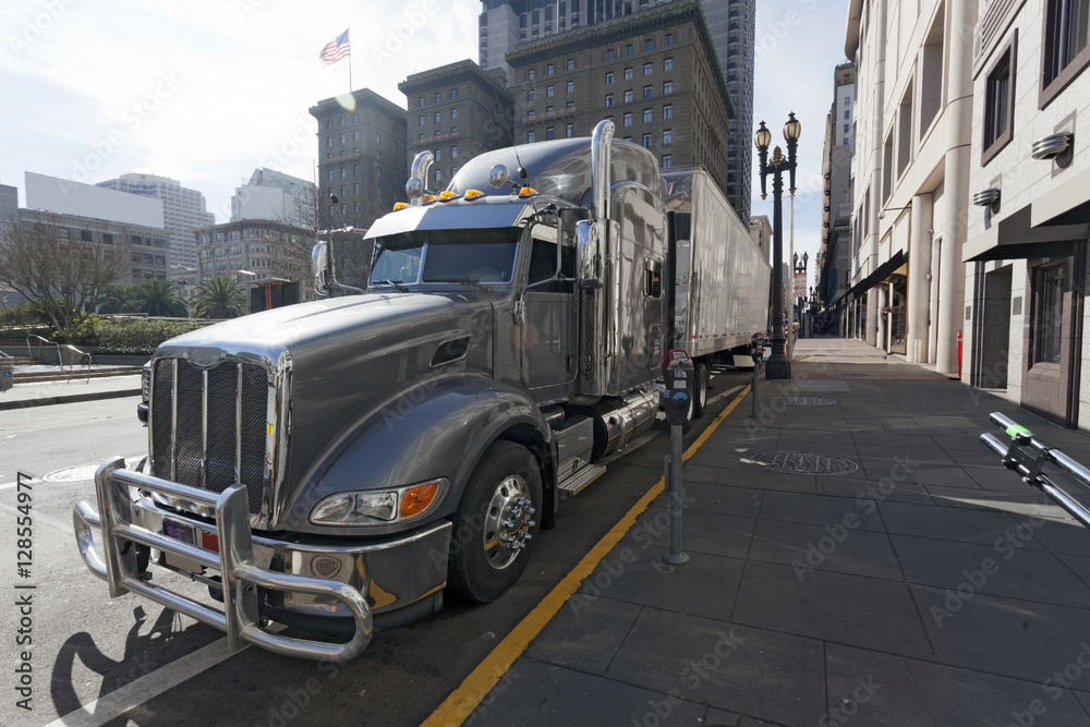 Side view of gray semi cab and trailer parked on urban street. Nobody ...