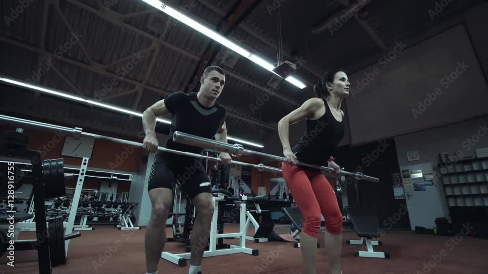 Strong athletic couple working out in a gym together lifting weights ...