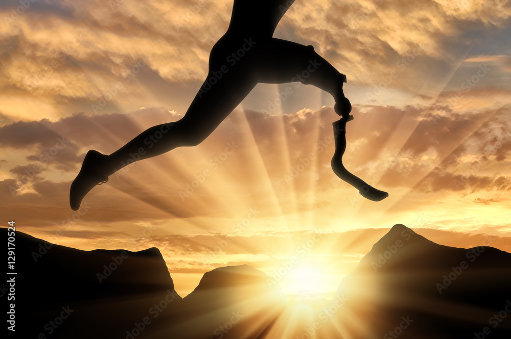 Disabled athlete with prosthetic leg jumping across rock on sunset ...