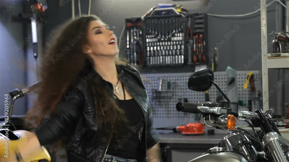 Young female biker dancing on the chopper at the mototrcycle workshop ...
