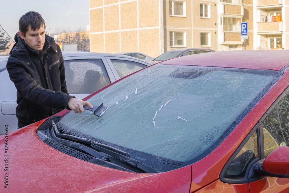 Man is scraping ice from frozen windshield window of car in winter ...